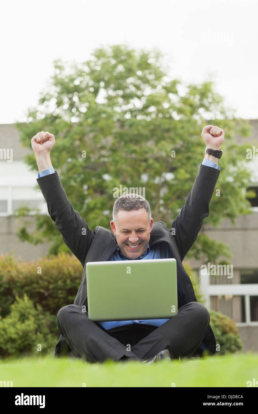 Excited cheering professor sitting outside on campus using his laptop ...