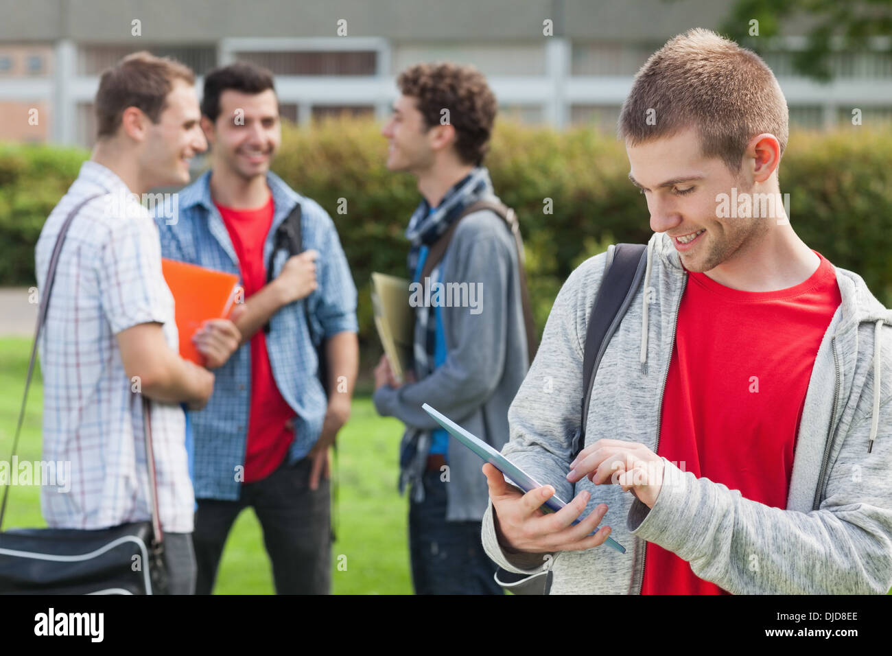 Cheerful male student using his tablet in front of his classmates ...