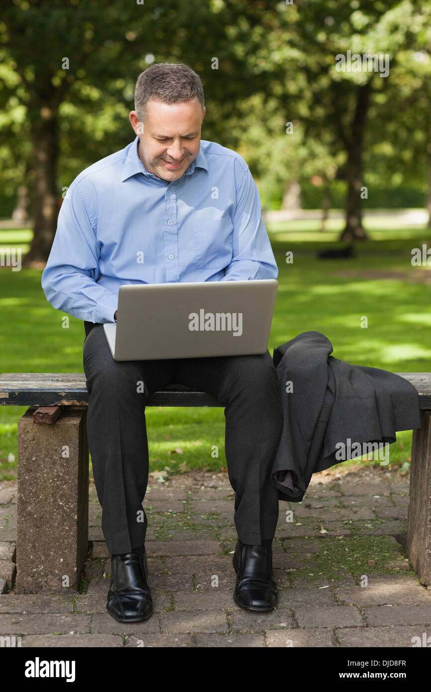 Happy lecturer sitting on bench using laptop on campus Stock Photo - Alamy