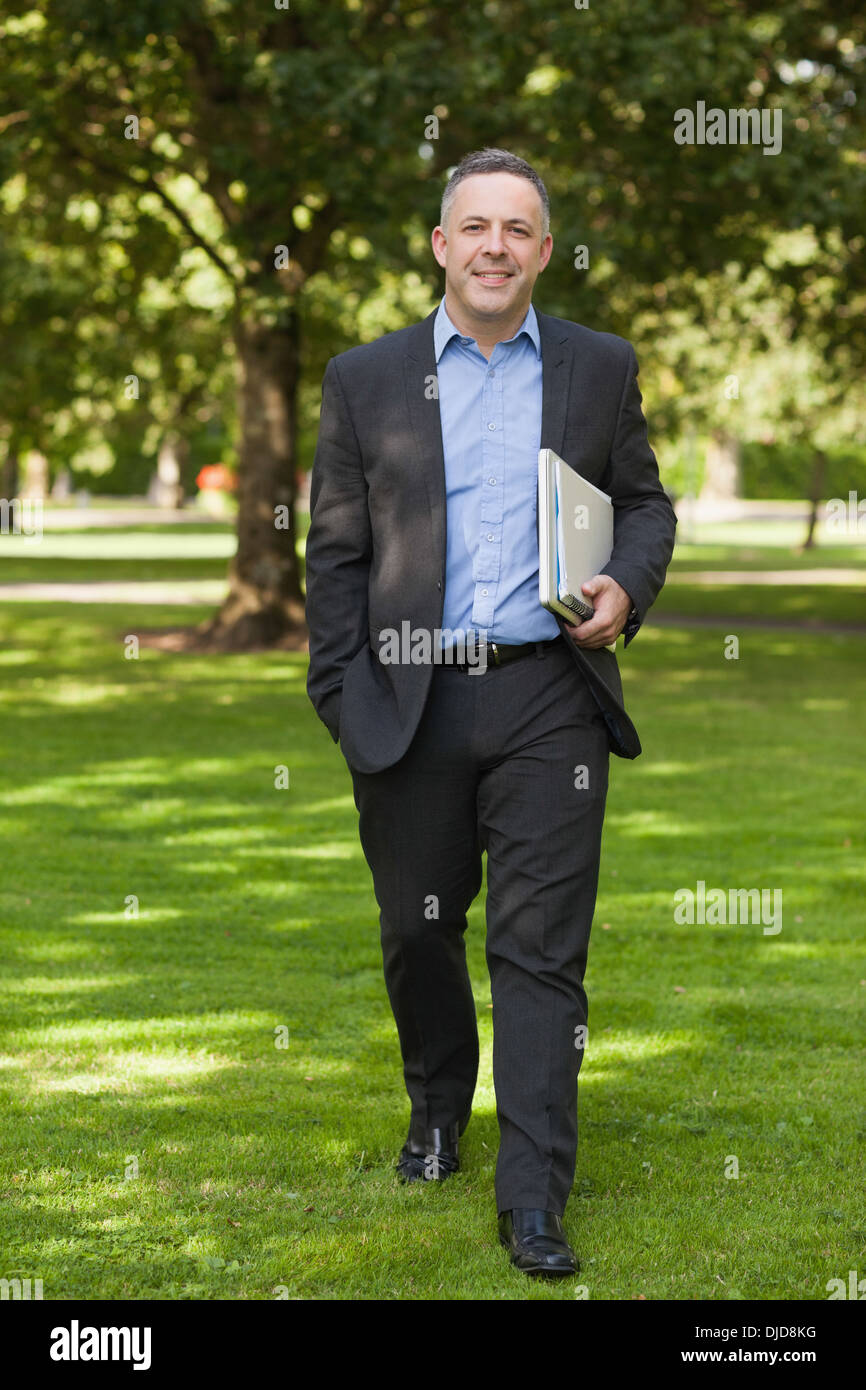 Happy professor walking across campus holding notepads Stock Photo - Alamy