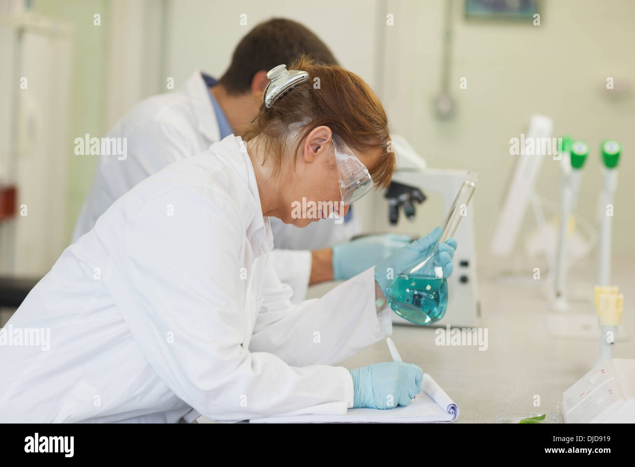 Female scientist leaning on a desk writing on a clipboard Stock Photo ...