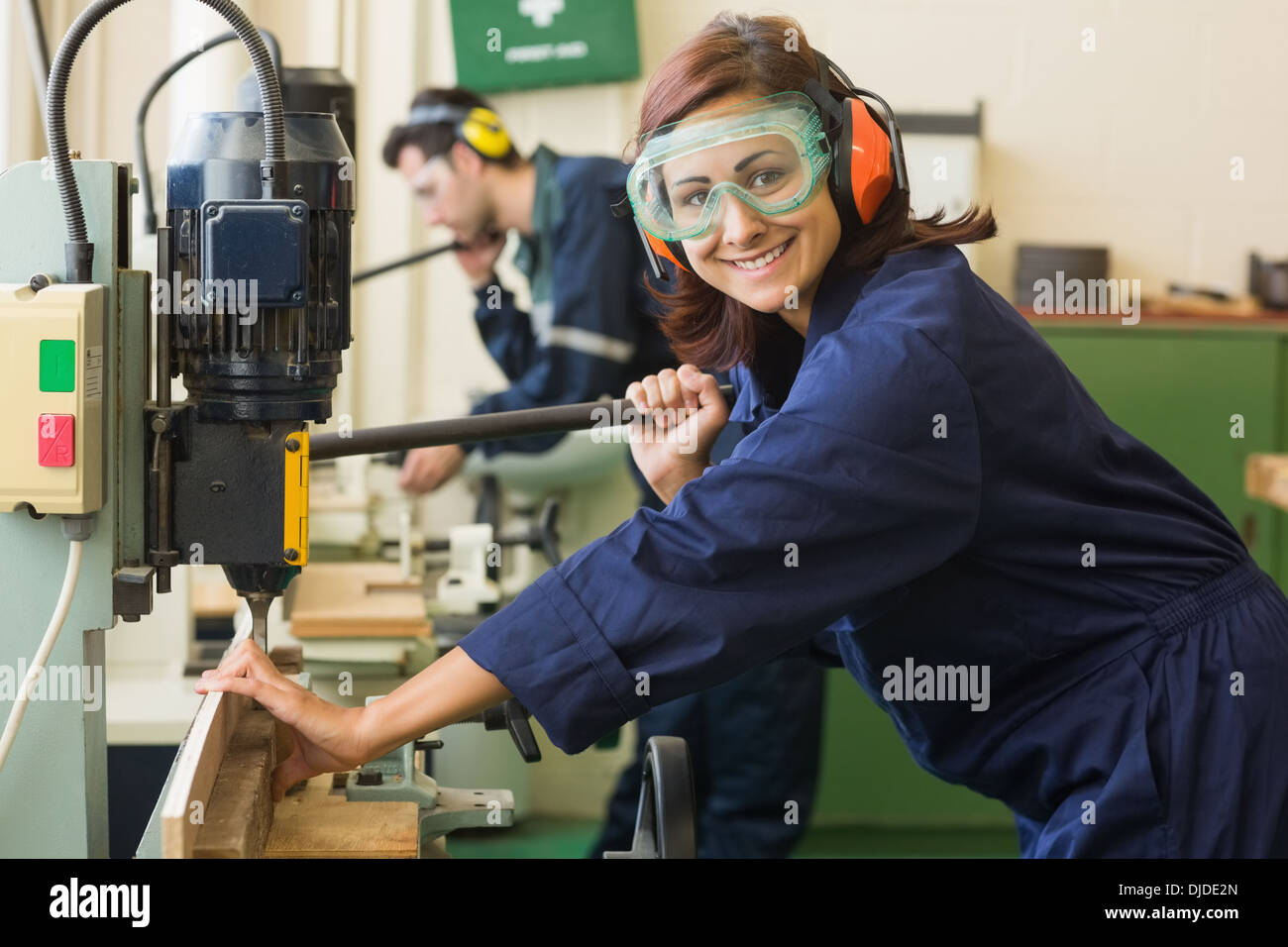 Smiling trainee with safety glasses drilling wood Stock Photo - Alamy