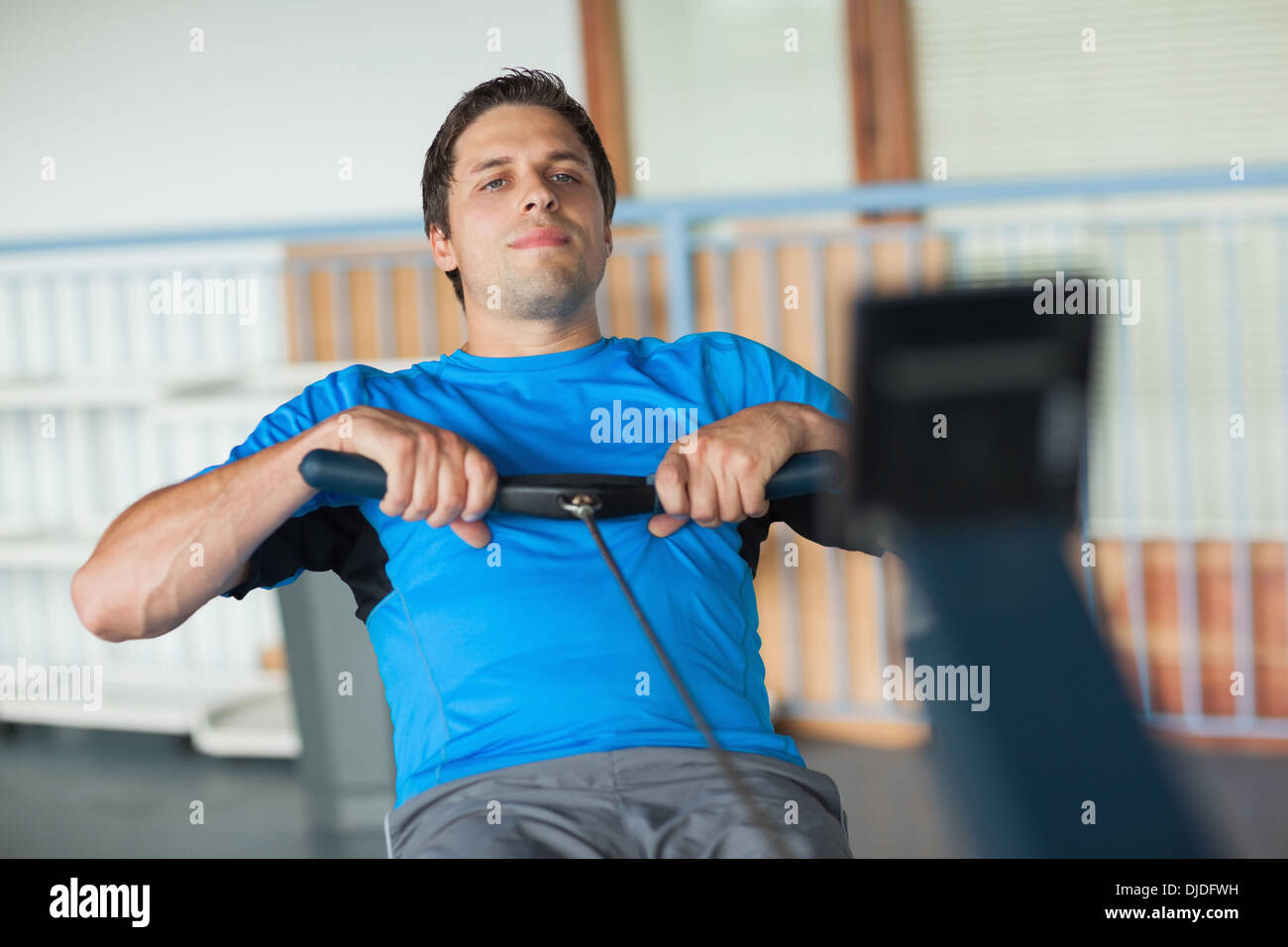 Determined young man working out on row machine Stock Photo - Alamy