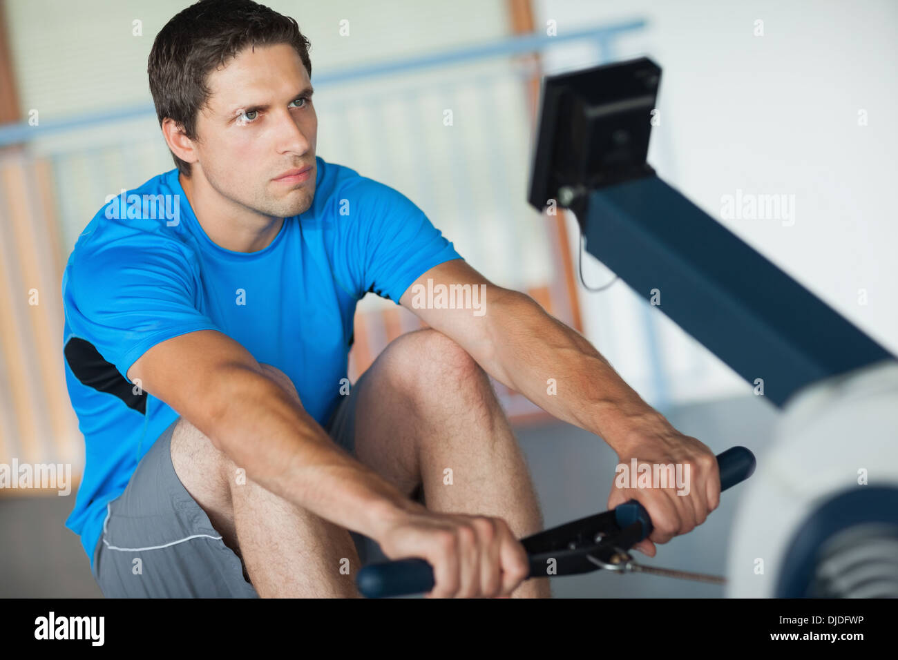 Determined young man working out on row machine Stock Photo - Alamy