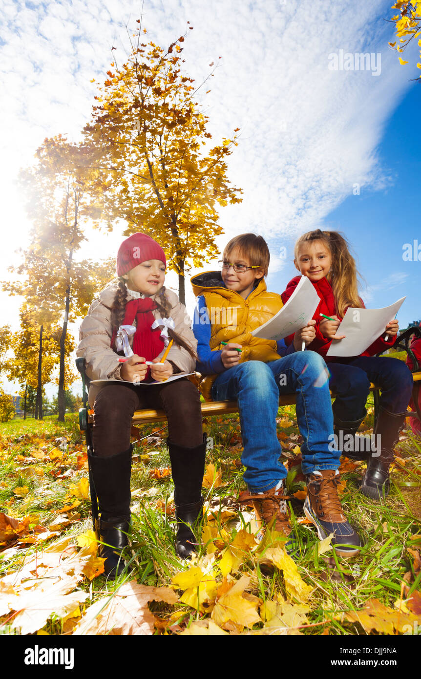 Group of three kids, friends, boy and girls, sitting on the bench in ...