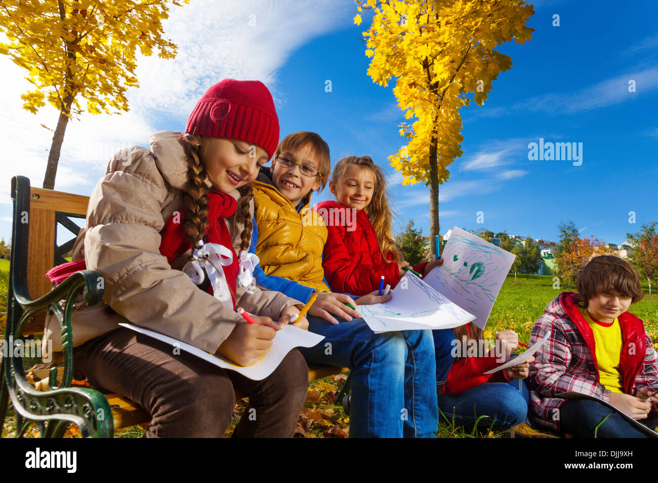 Group of kids sitting on the bench in the park under the autumn maple ...