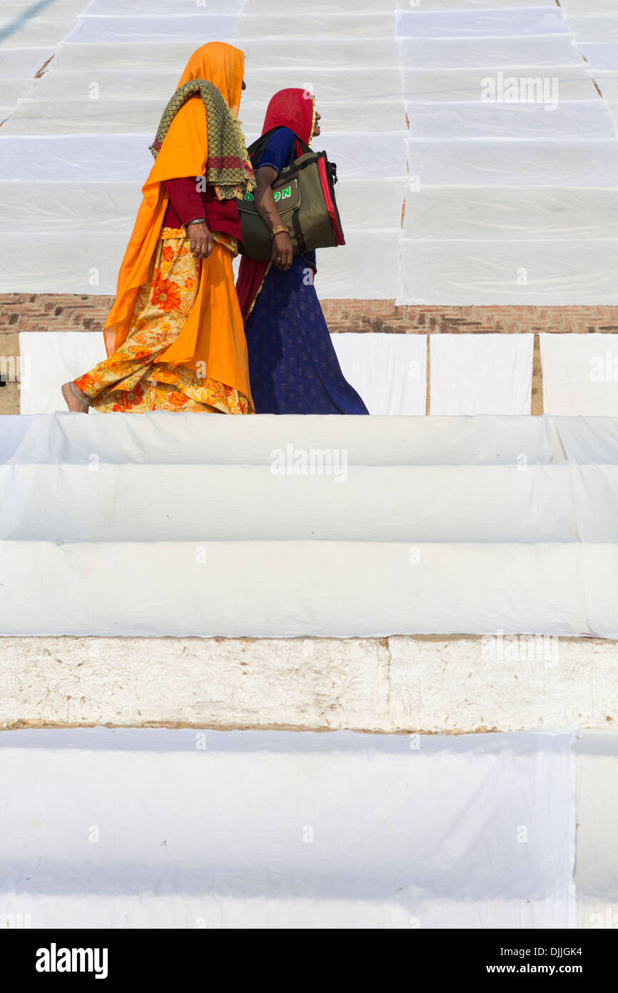 Two women walk along the sheets laid out to dry on the steps located on ...