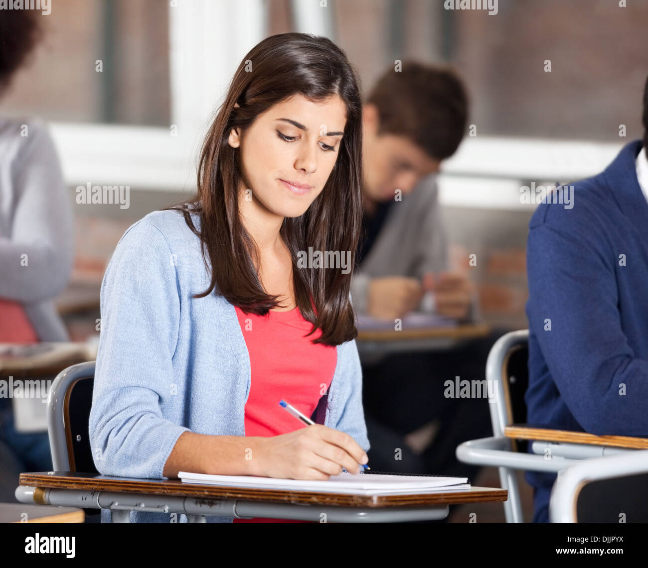Woman Writing On Book At Desk In Classroom Stock Photo - Alamy