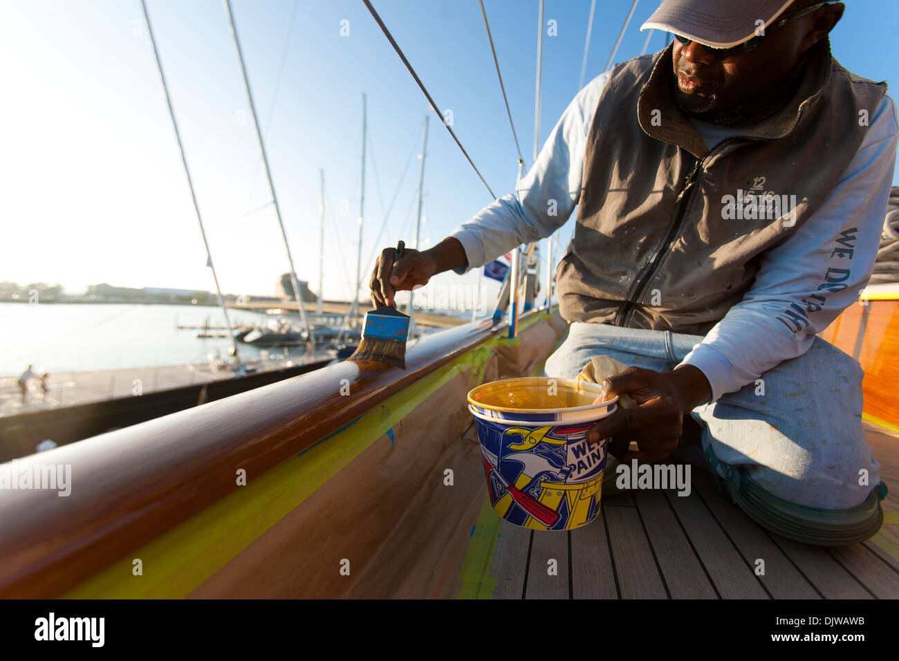 A varnisher varnishes a teak cap rail on a sailing yacht at Newport ...