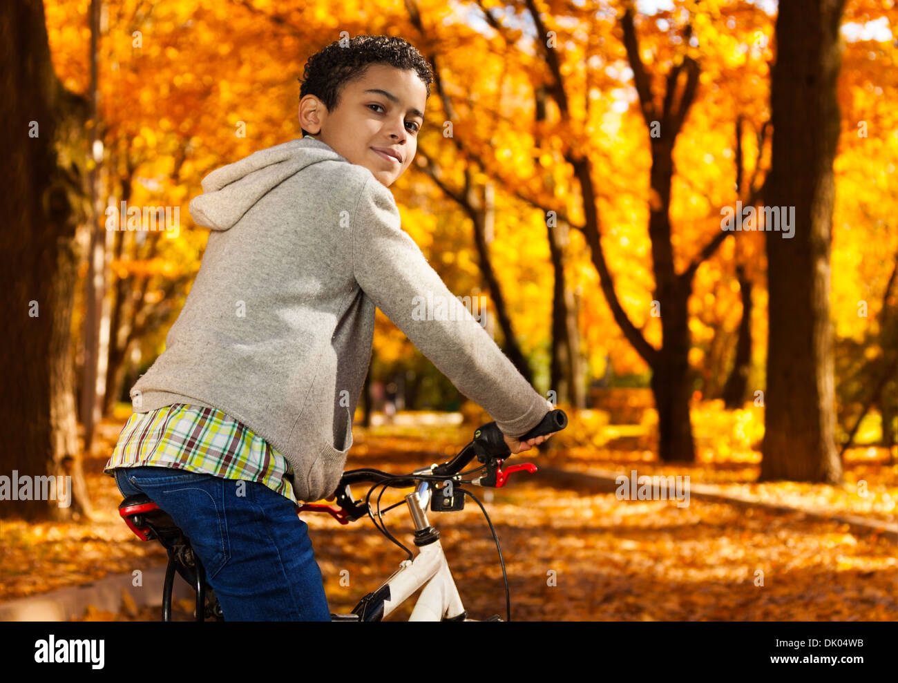 Close portrait of nice black boy riding a bicycle in the autumn park ...