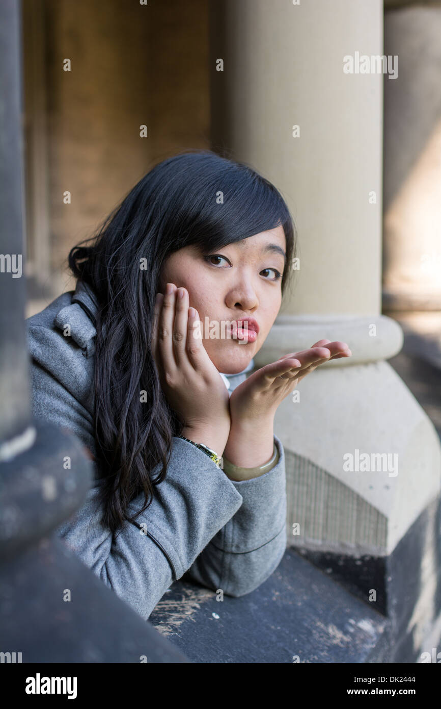 young woman leaning forward next to stone pillars blowing a kiss Stock ...