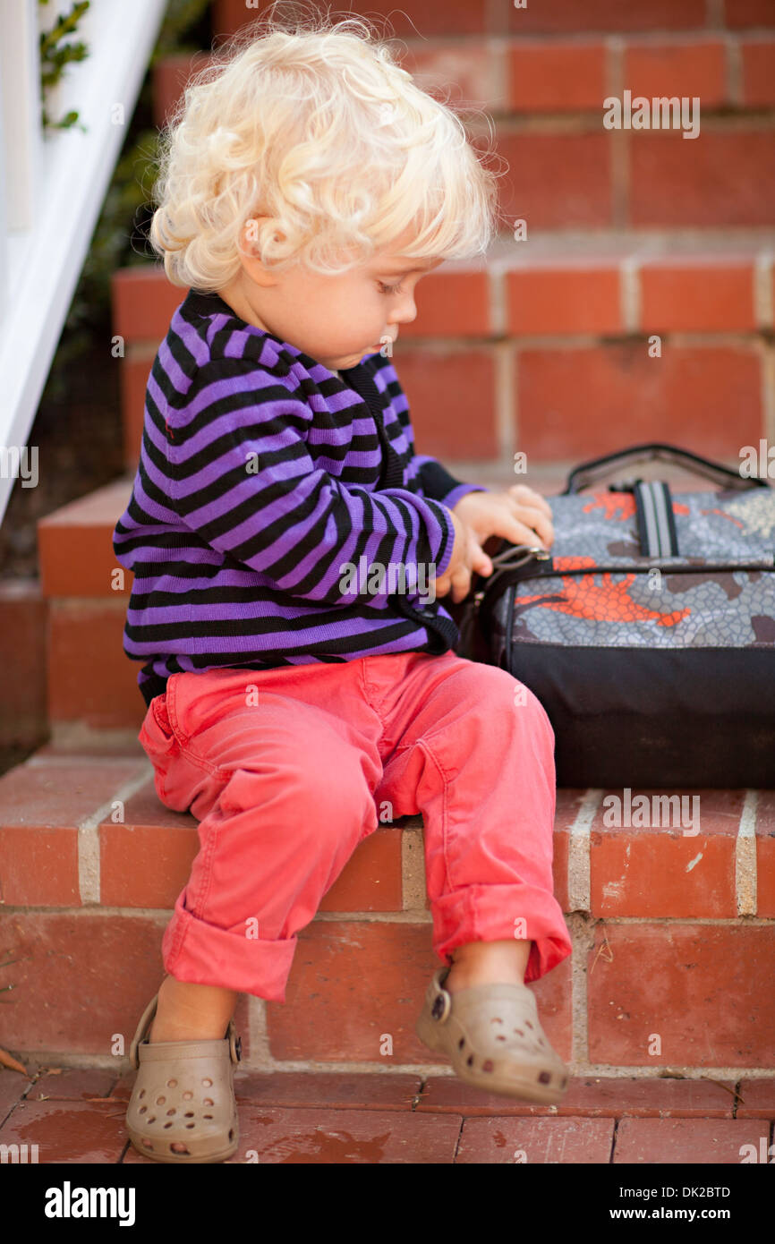 Blonde toddler school boy with curly hair with backpack on brick steps ...