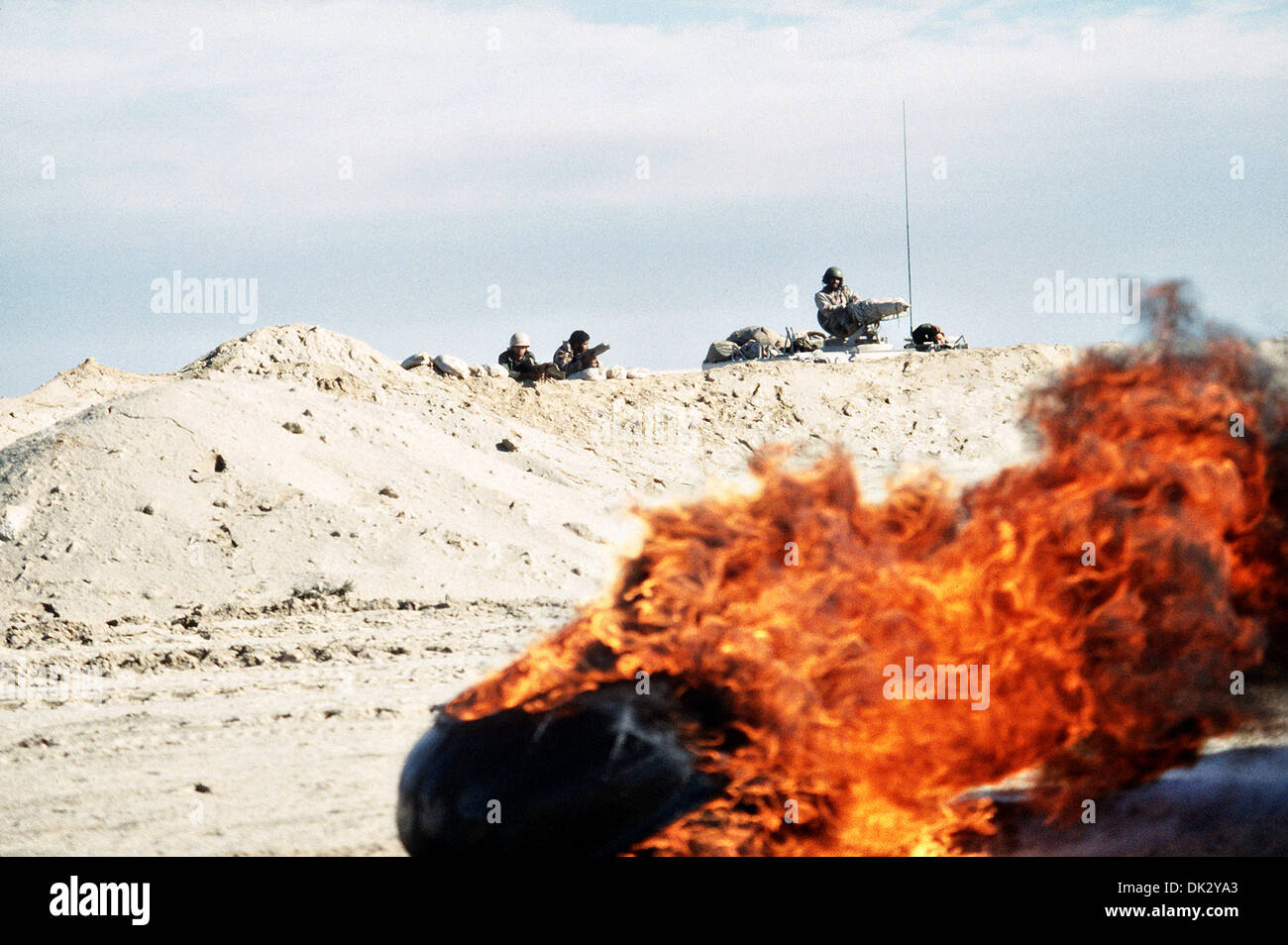 Armored units wait along a sand berm as destroyed vehicles burn during ...
