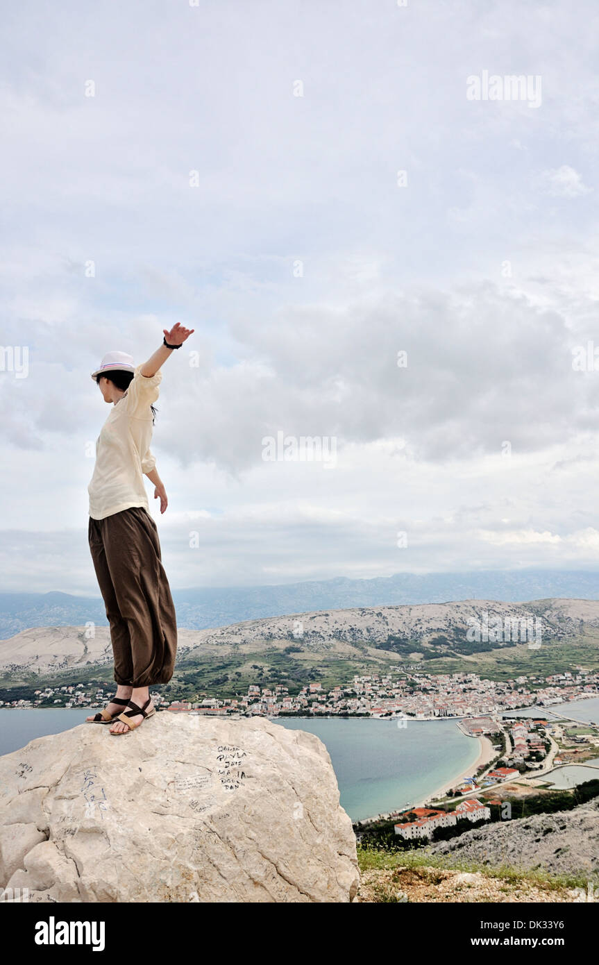 Mid adult woman with outstretched arms standing on rock overlooking ...