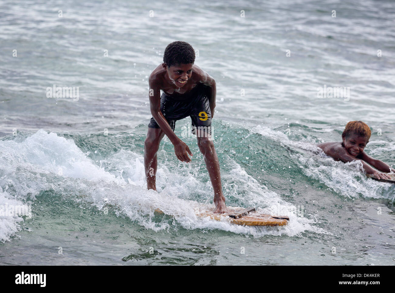 Young Papuan boys surfing on piece of wood on the Pacific coast near ...