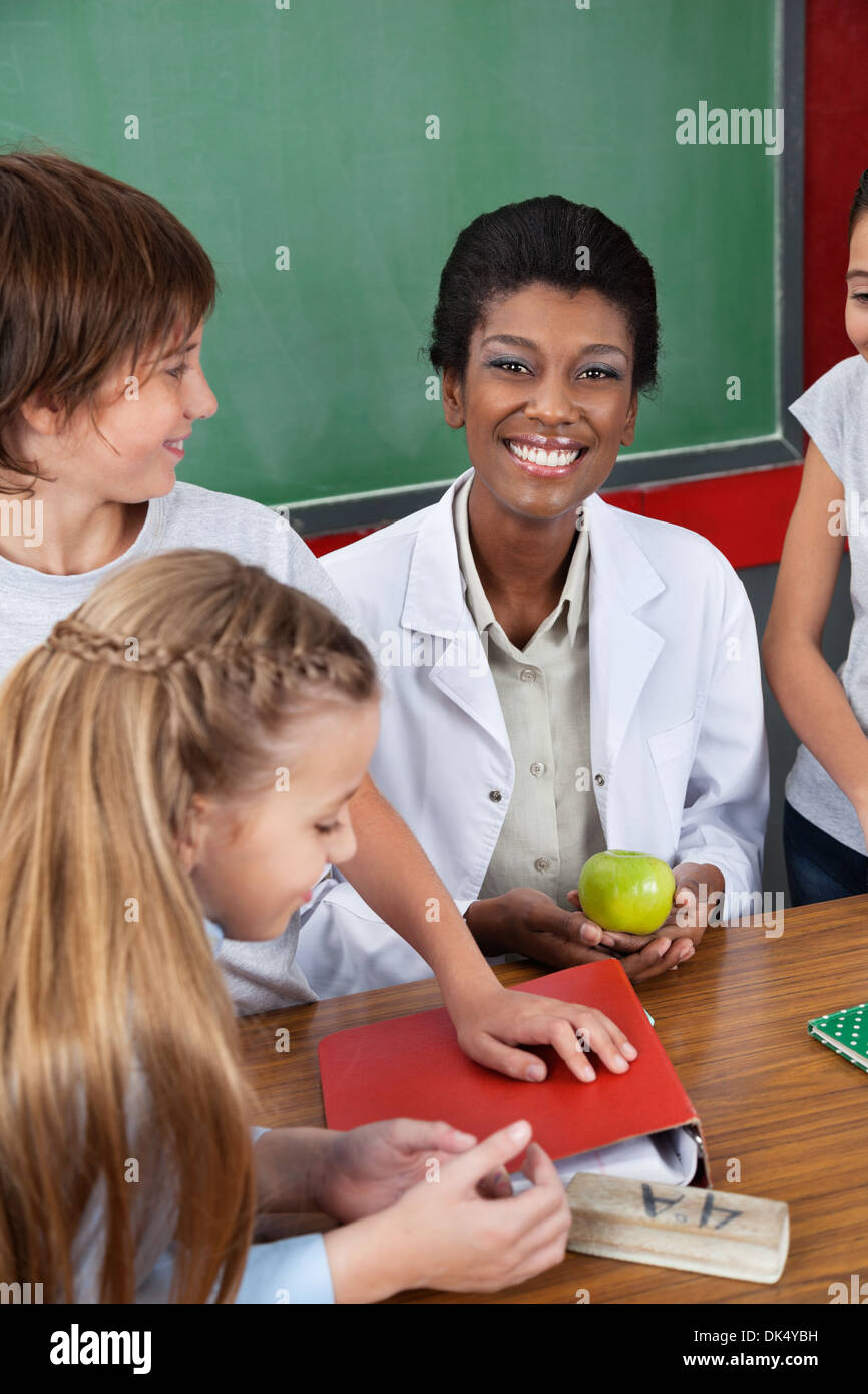 Teacher Holding Apple With Students Standing At Desk Stock Photo - Alamy