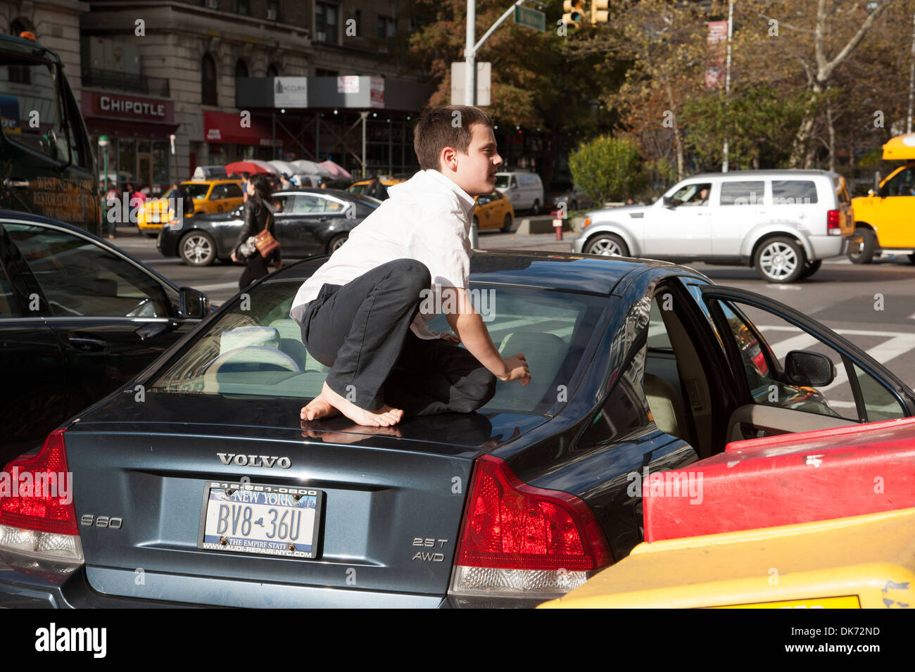 Boy climbing on rear window of a Volvo car which is parked on the side ...