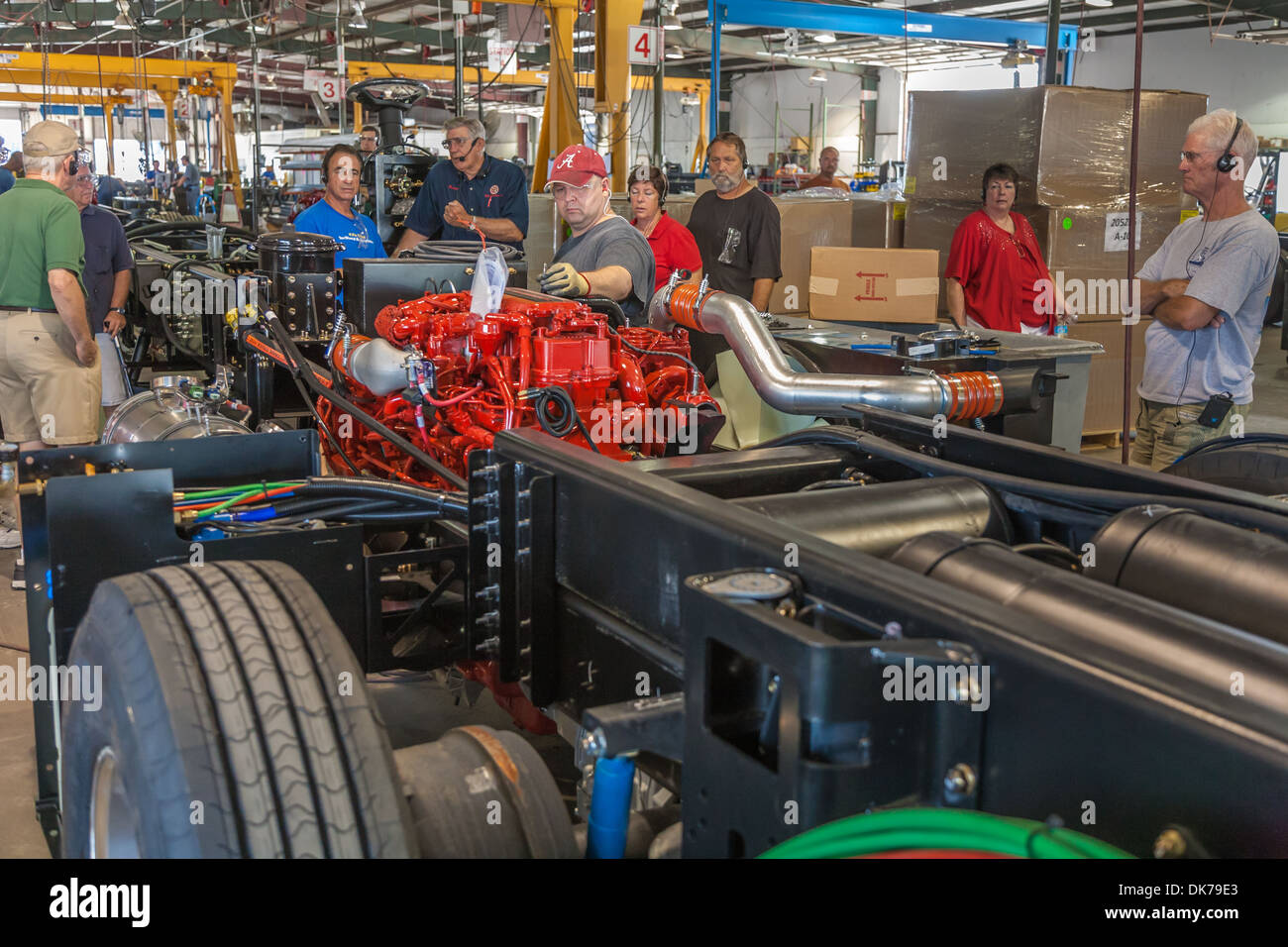 Visitors watch worker install a Cummins ISL diesel engine onto chassis ...