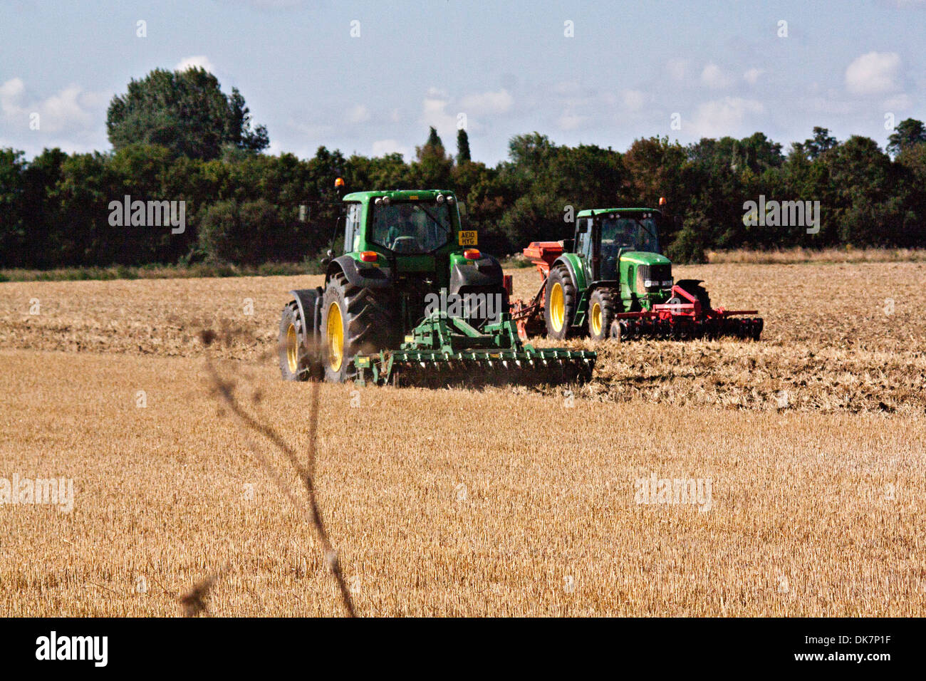 two John Deere tractors passing while harrowing and seed drilling ...