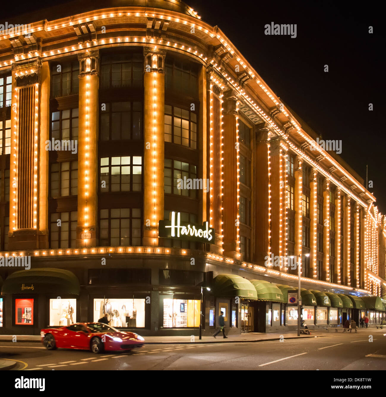 Harrods department store. Facade illuminated at night. Ferrari passes ...