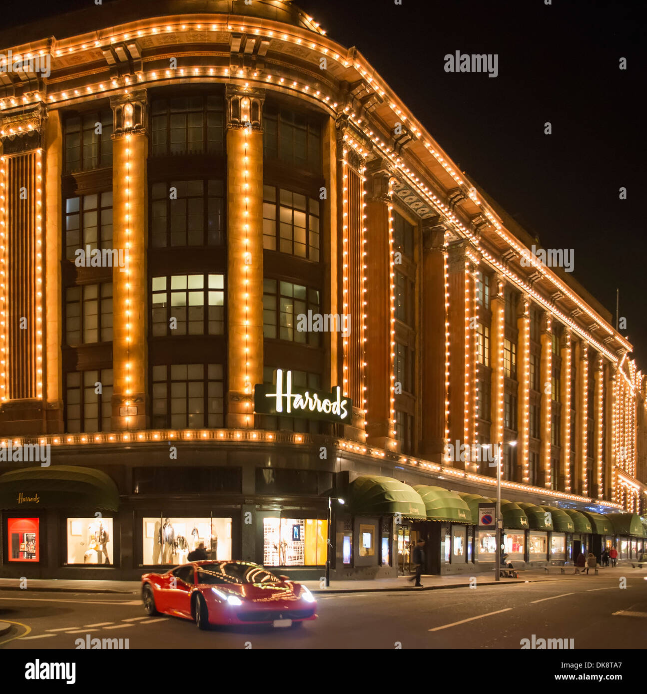 Harrods department store. Facade illuminated at night. Ferrari passes ...