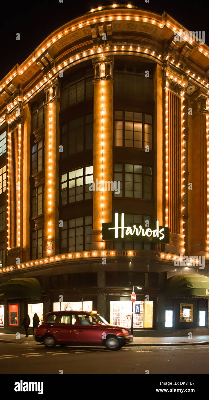 Harrods department store. Facade illuminated at night. Taxi passes in ...