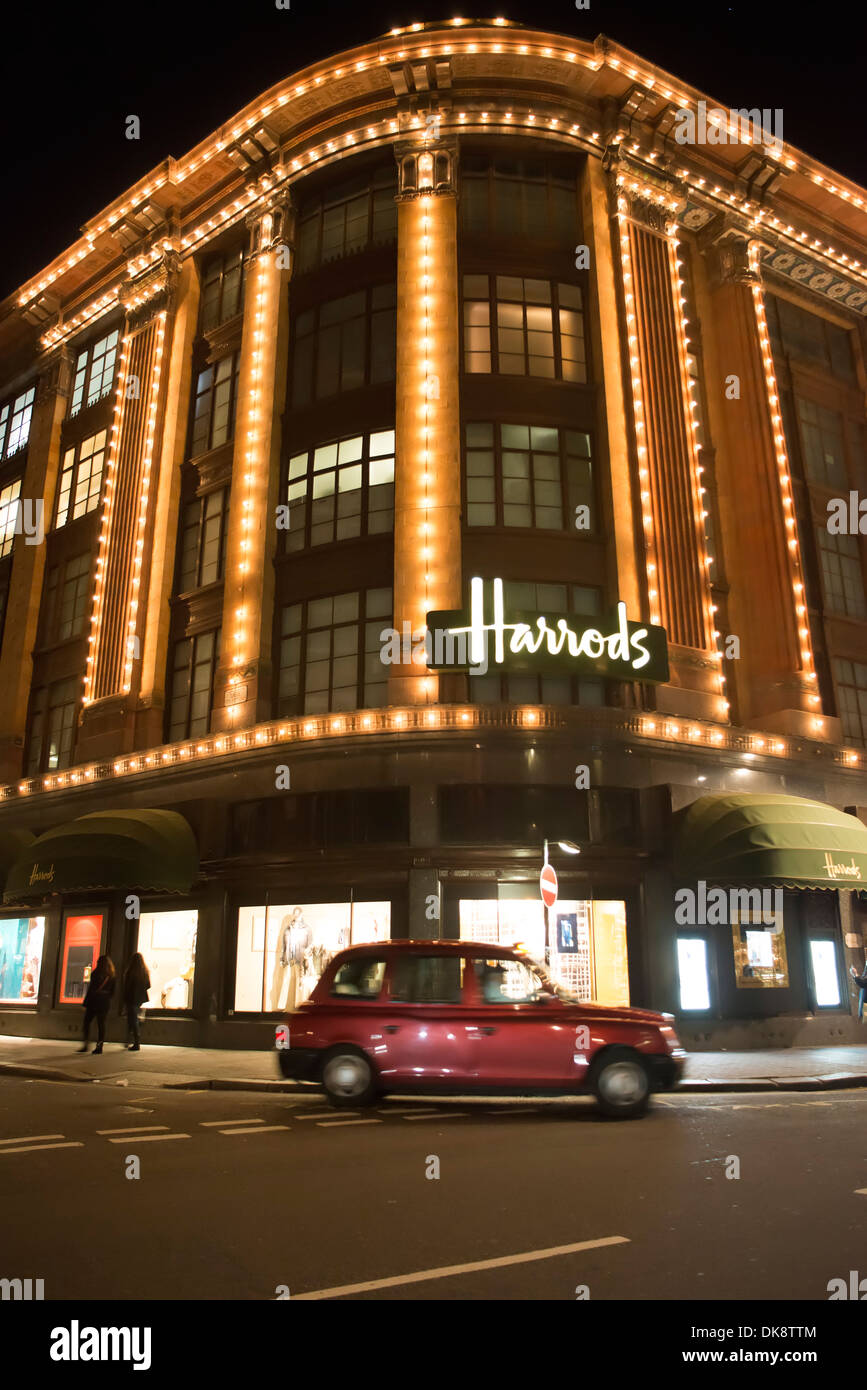 Harrods department store. Facade illuminated at night. Taxi passes in ...