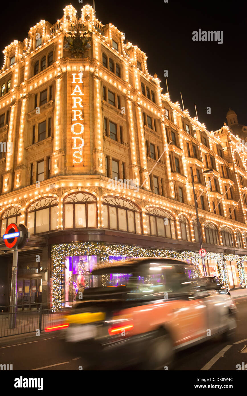 Harrods department store. Facade illuminated at night. Taxi passes in ...