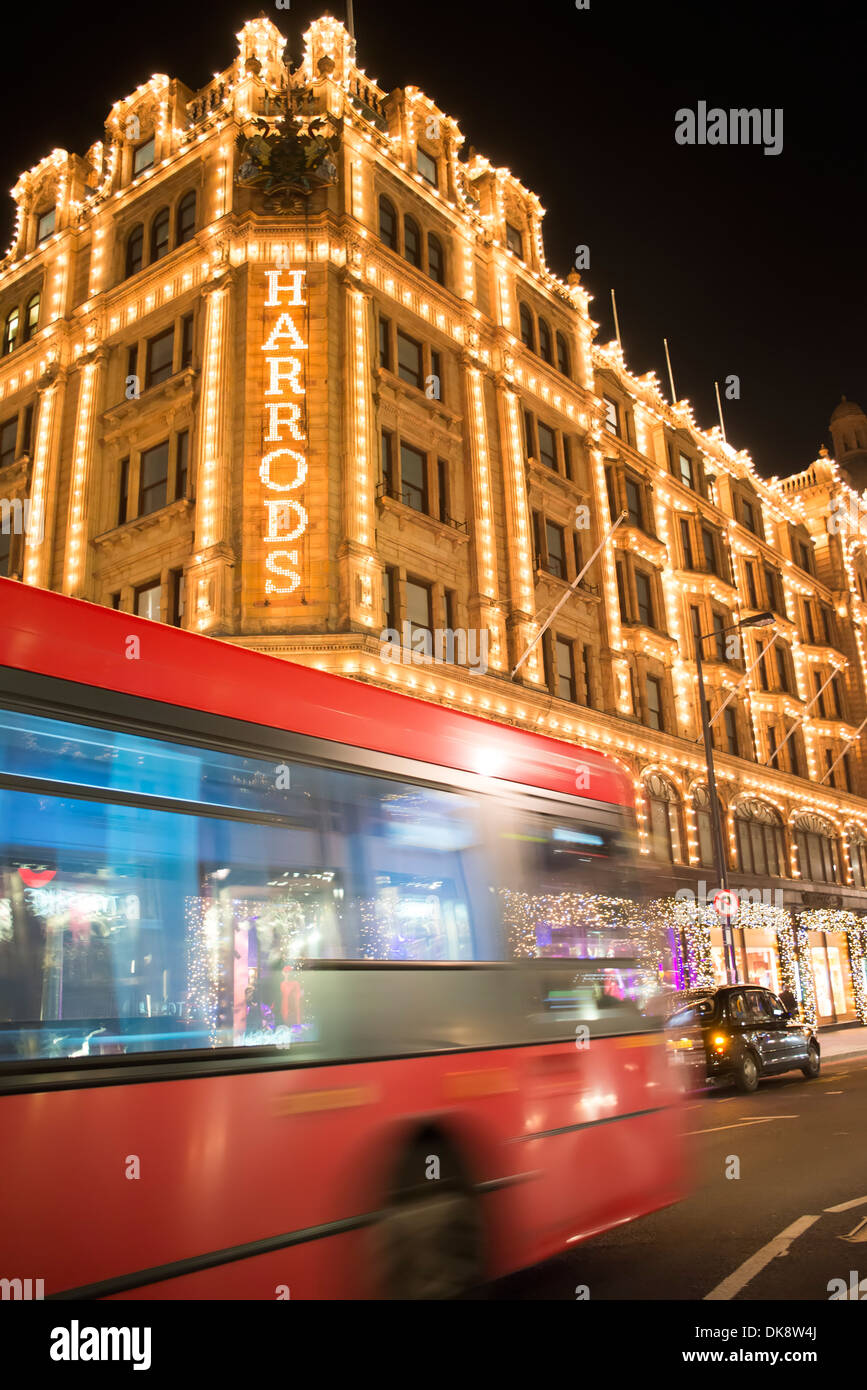 Harrods department store. Facade illuminated at night. Red bus passes ...