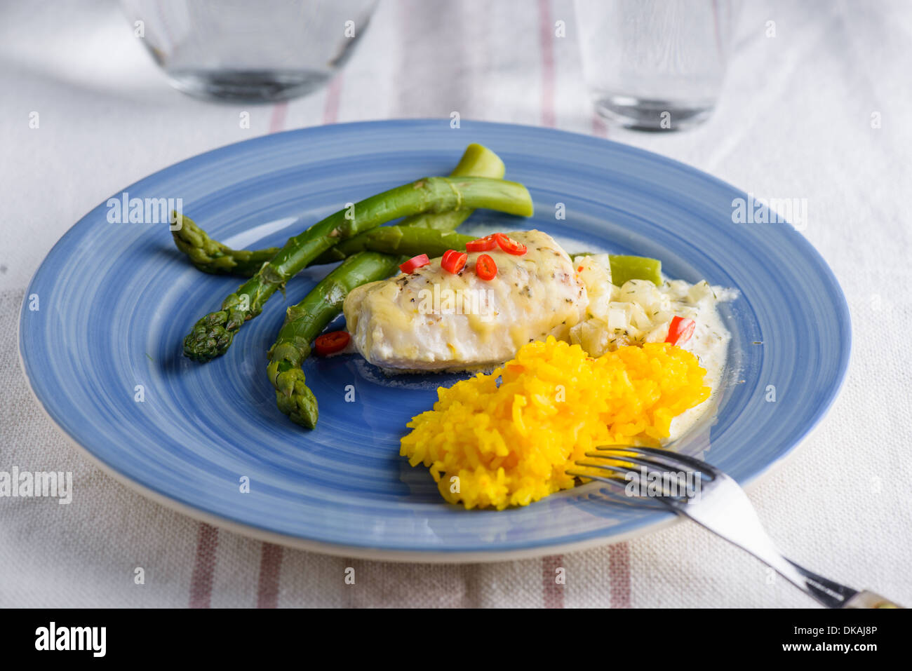 White fish with saffron rice and some cheese on top and aspargus on the ...