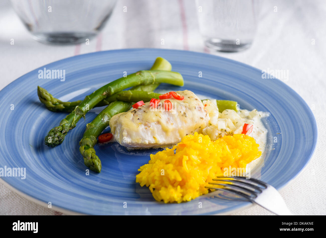 White fish with saffron rice and some cheese on top and aspargus on the ...