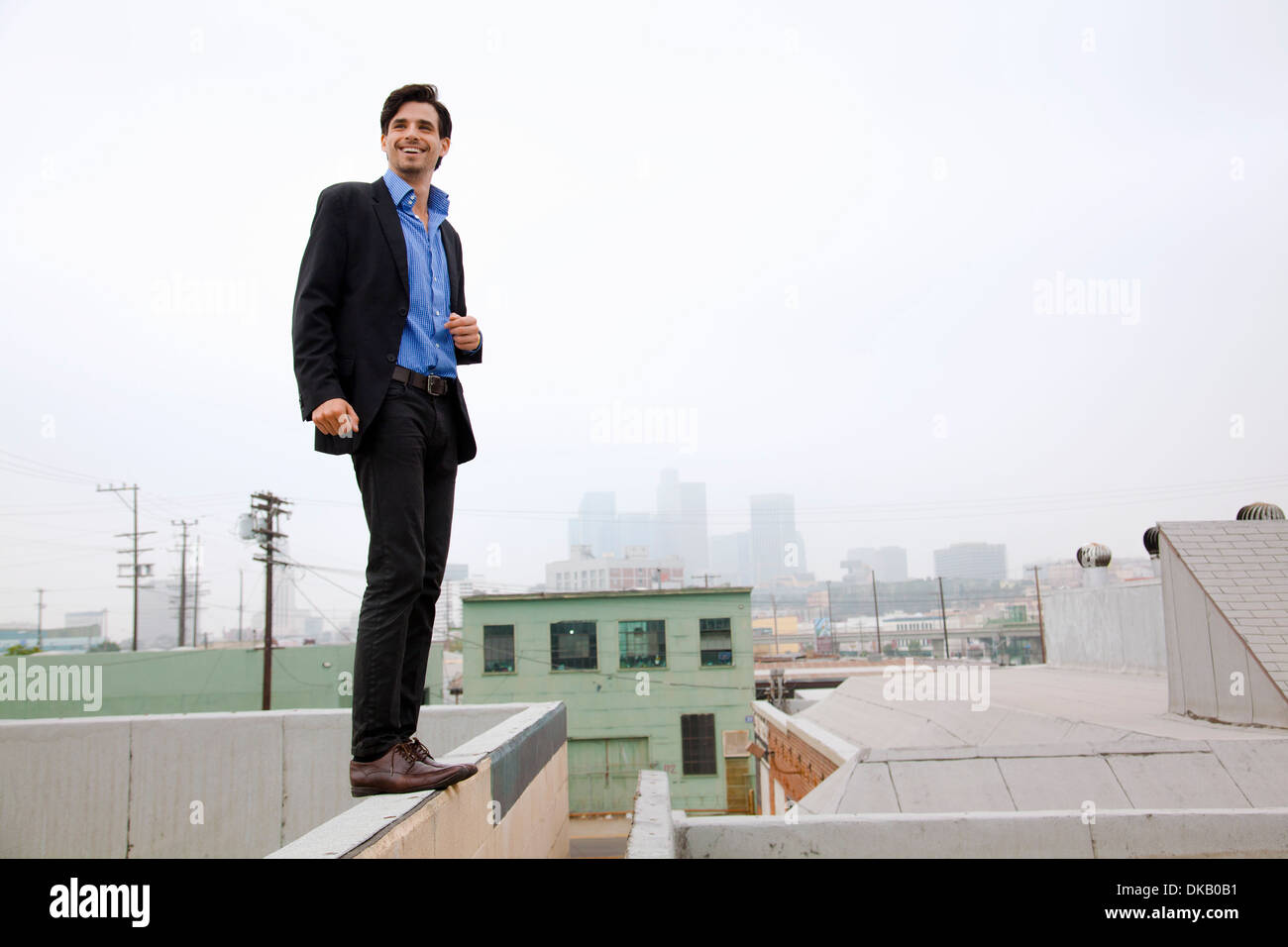 Young man standing on wall on city rooftop Stock Photo - Alamy
