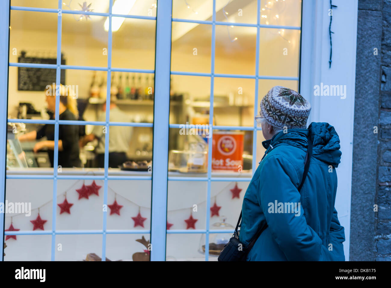 Elderly woman wearing blue coat and hat looking into shop window late ...