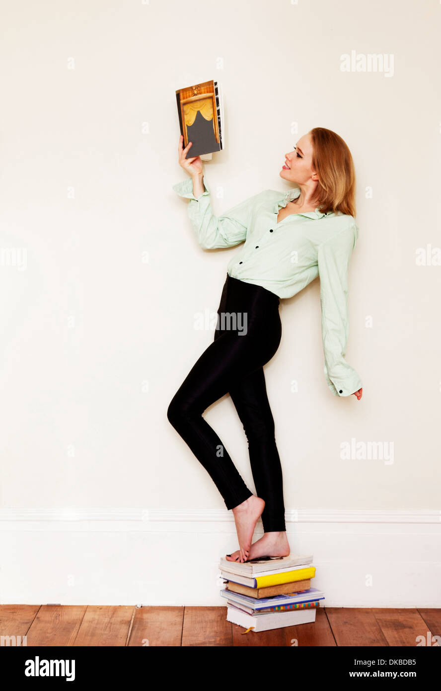 Young woman standing on pile of books, reading Stock Photo - Alamy