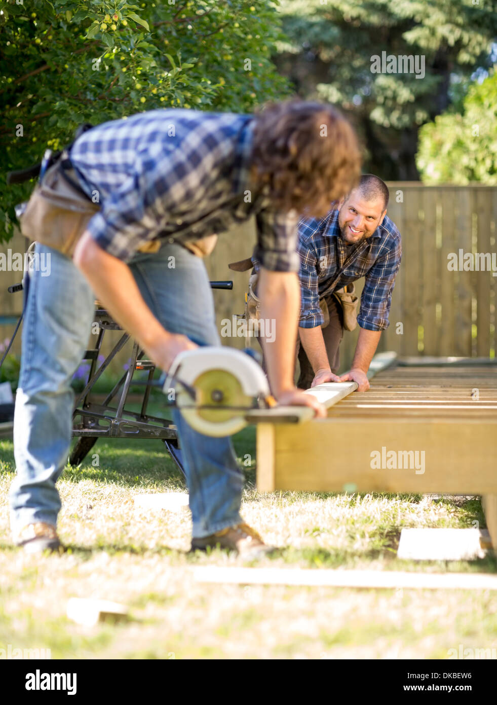 Carpenter Assisting Coworker In Cutting Wood With Handheld Saw Stock ...