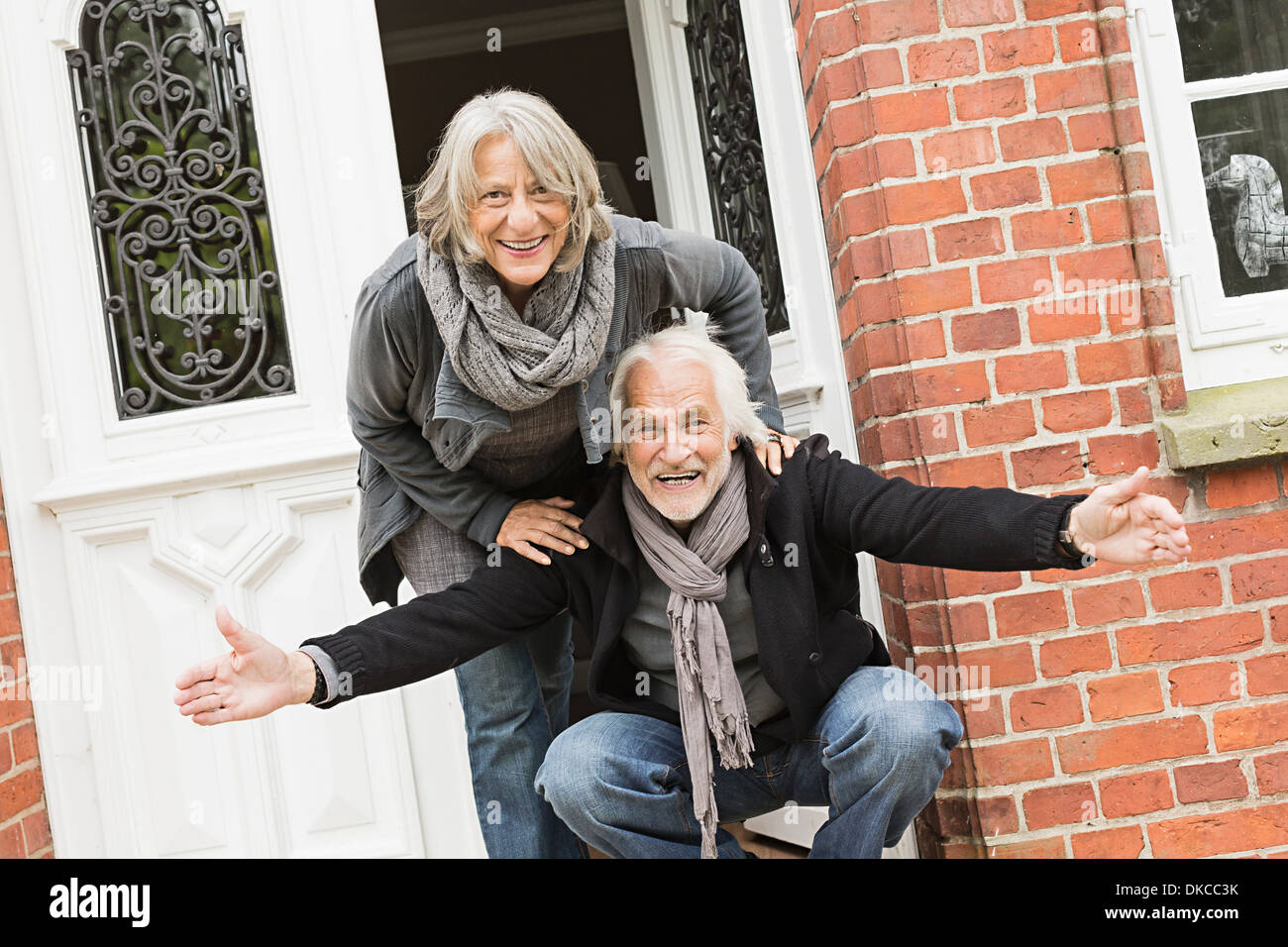 Senior couple by front door, man crouching with open arms Stock Photo ...