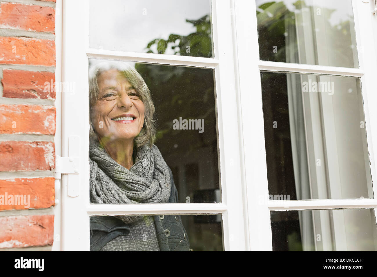 Senior woman looking through window Stock Photo - Alamy