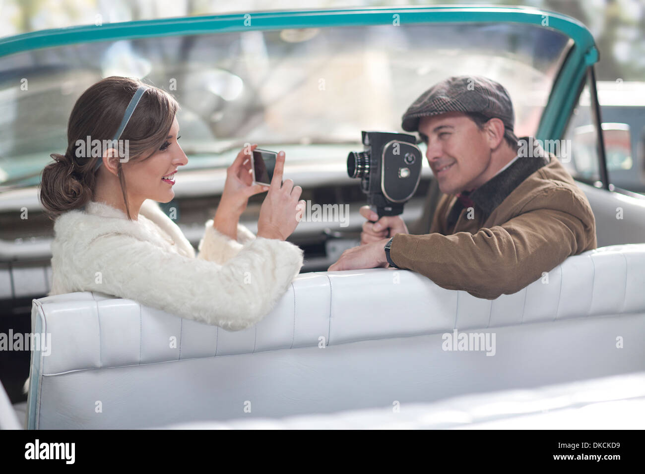 Couple in convertible filming and photographing each other with modern ...