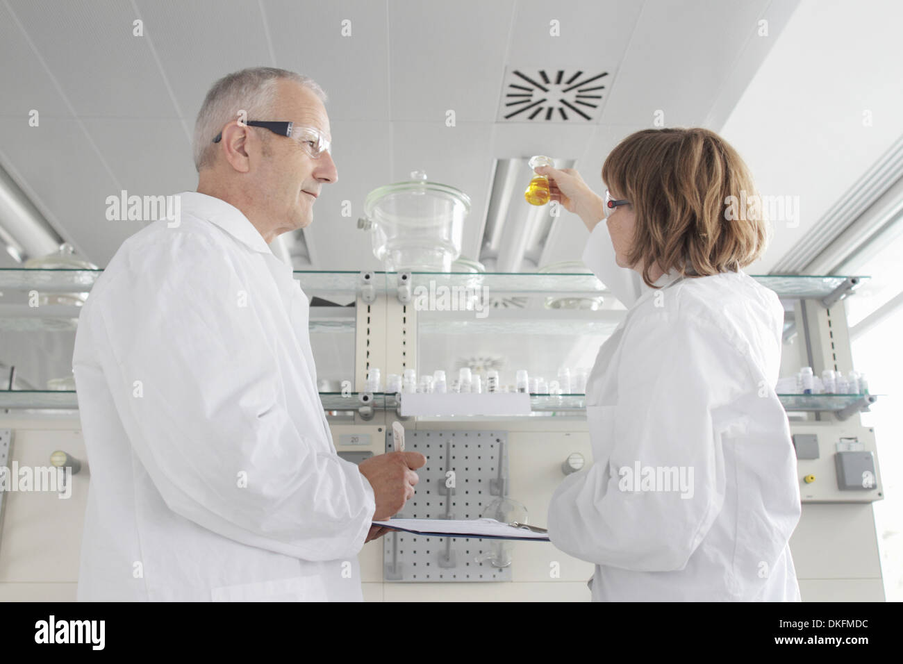 Scientists working in laboratory, looking at yellow liquid in vial ...