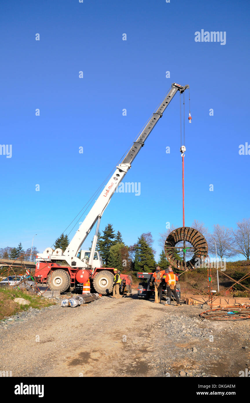 Workers offload rebar cylinder shape off flatbed truck, using a crane ...