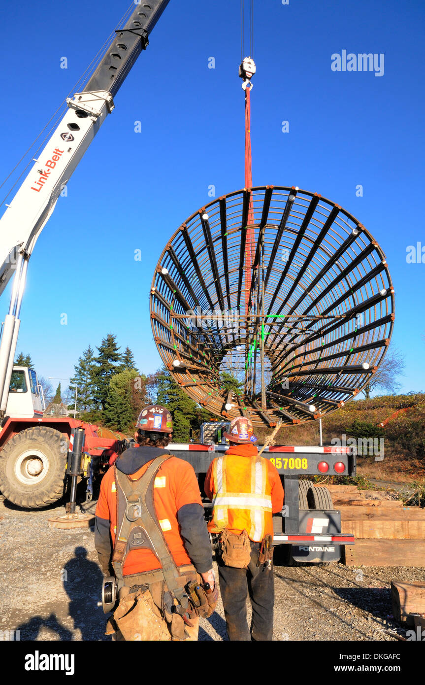 Workers offload rebar cylinder shape off flatbed truck, using a crane ...