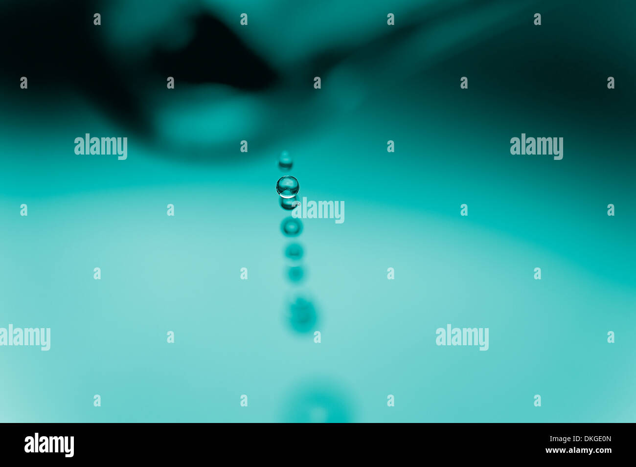 Water droplets dripping from a tap, with a single droplet in focus ...