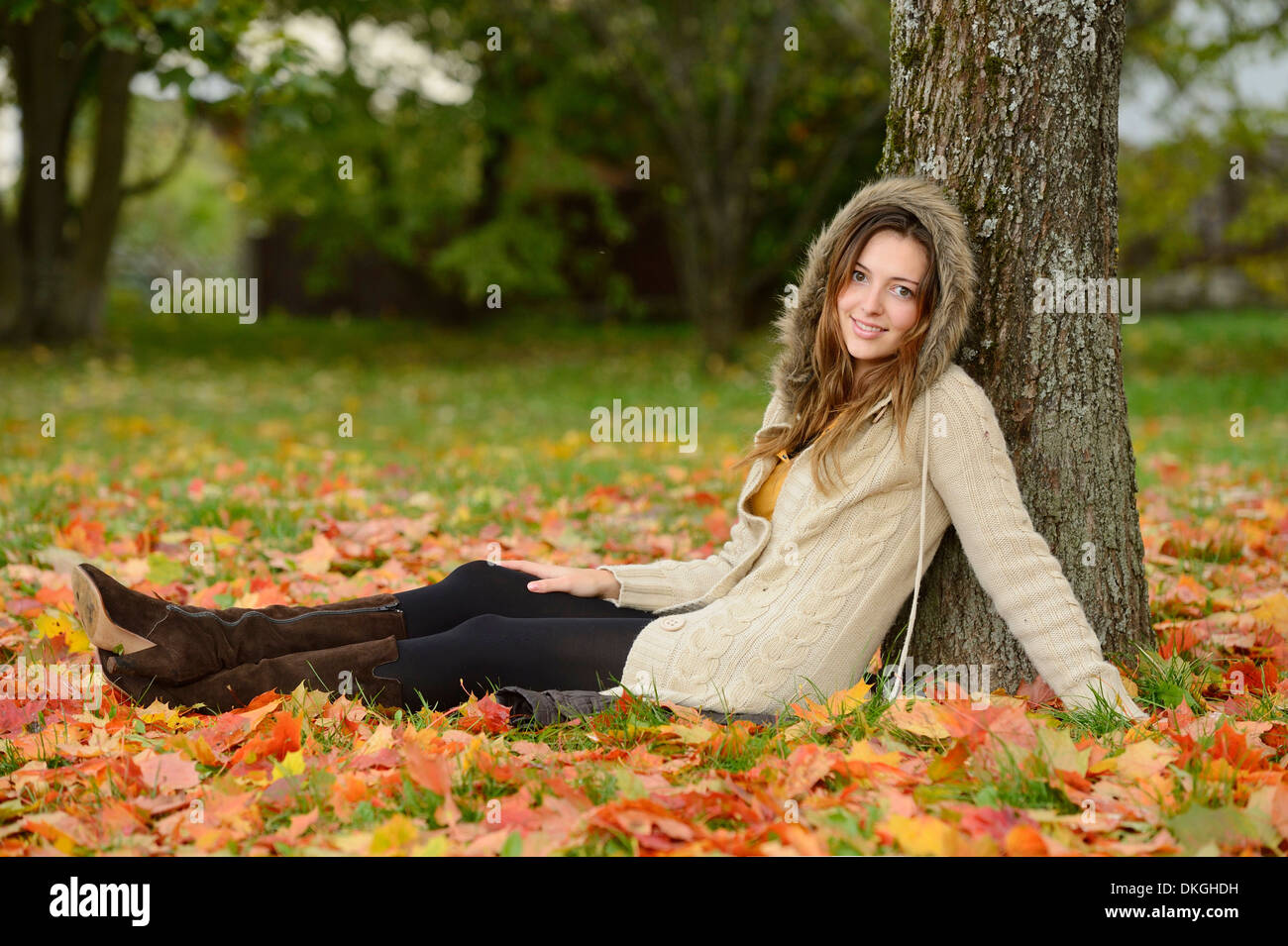 Smiling young woman sitting under a tree in autumn Stock Photo - Alamy