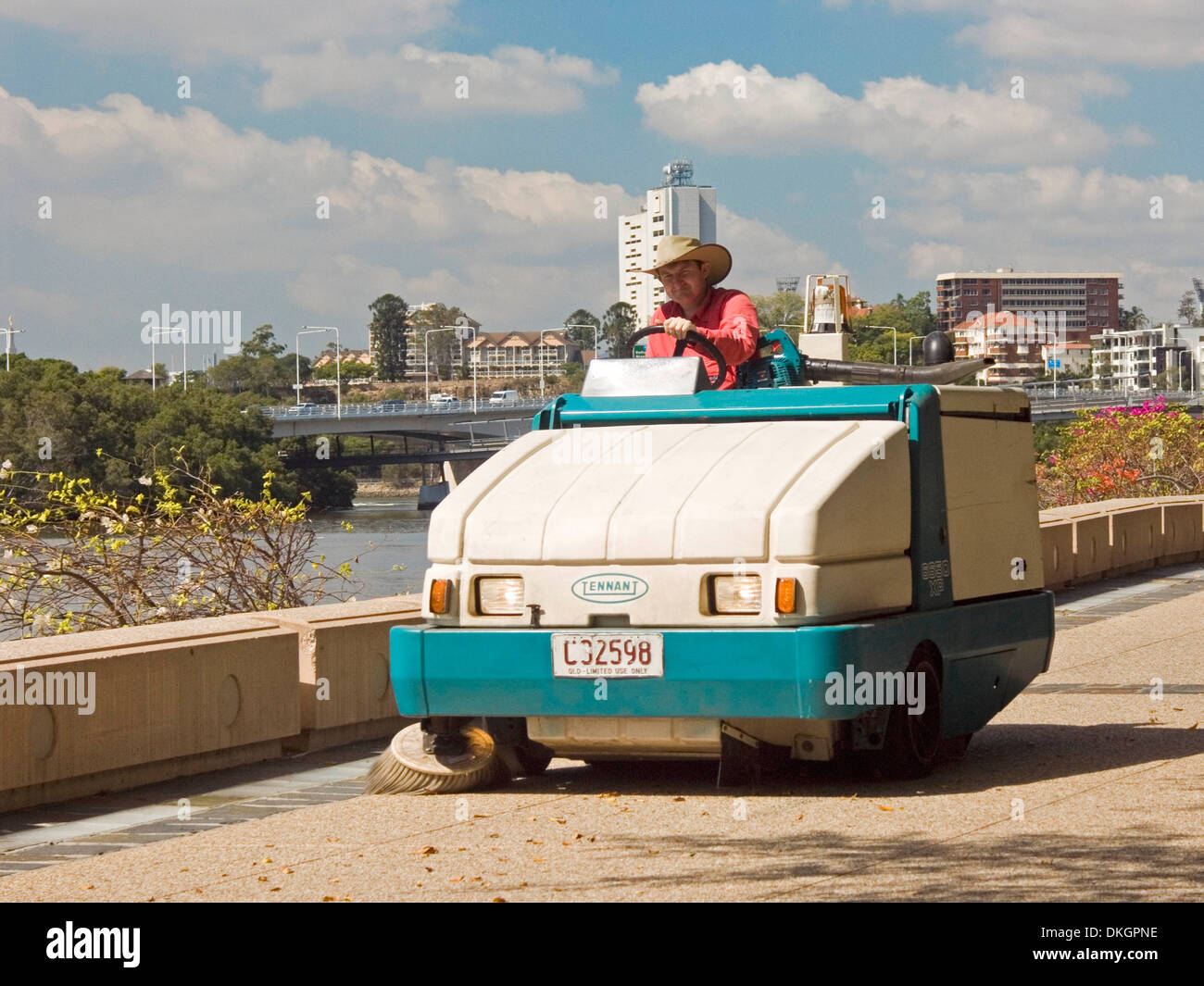 Man operating modern road / pathway sweeping machine beside river in ...