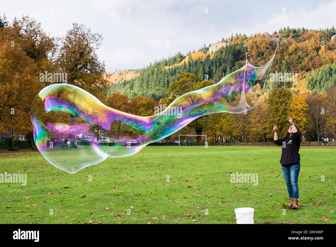 A woman makes a giant soap bubble with rainbow colours using a bubble wand in Betws-y-Coed ...
