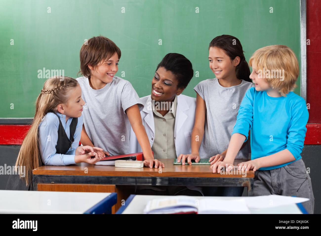Happy Teacher With Students Communicating At Desk Stock Photo - Alamy