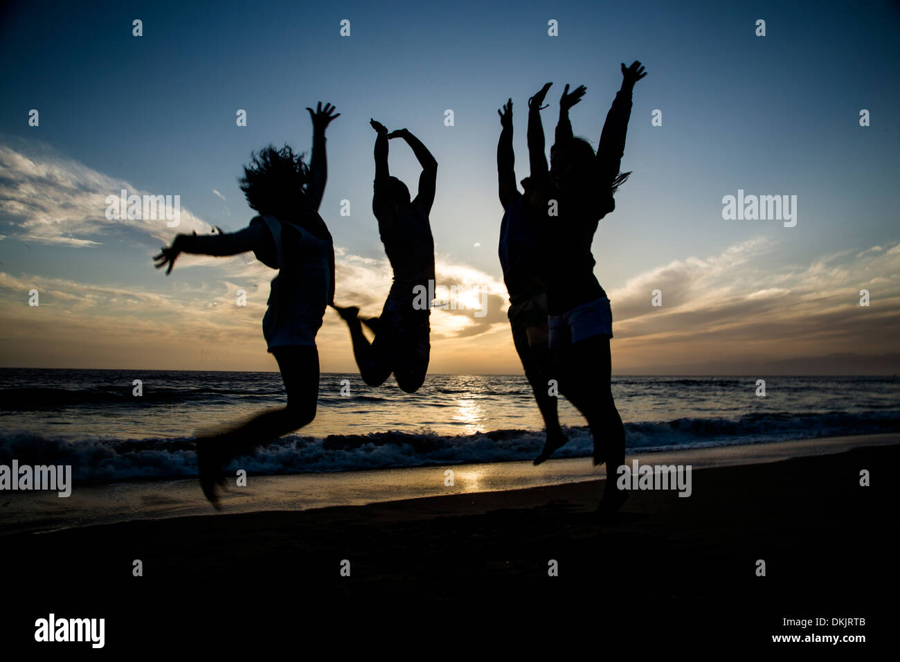 Two young couples jumping on beach at sunset Stock Photo - Alamy