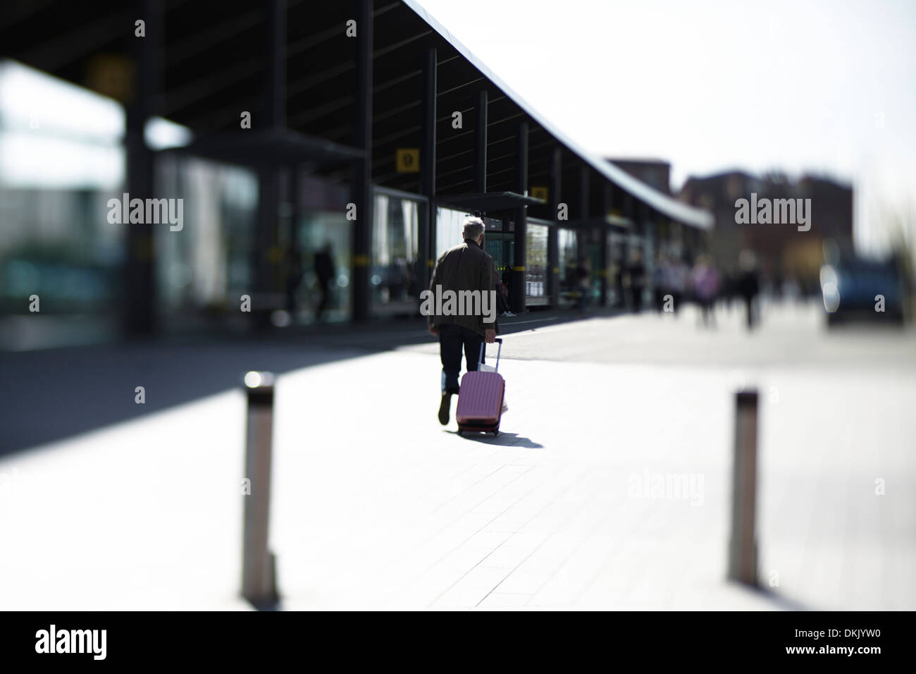 Man pulling suitcase alone by bus station Stock Photo - Alamy