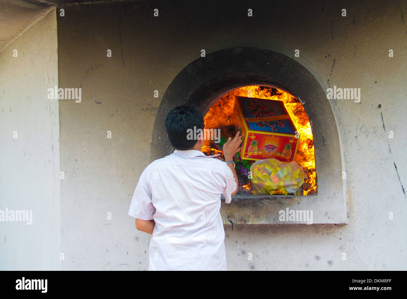 Chinese man putting paper offering into a ceremonial furnace during ...
