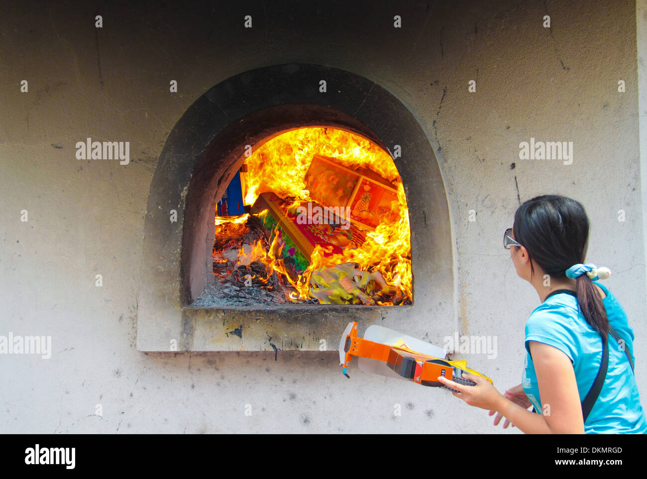 Chinese woman putting paper offering into a ceremonial furnace during ...